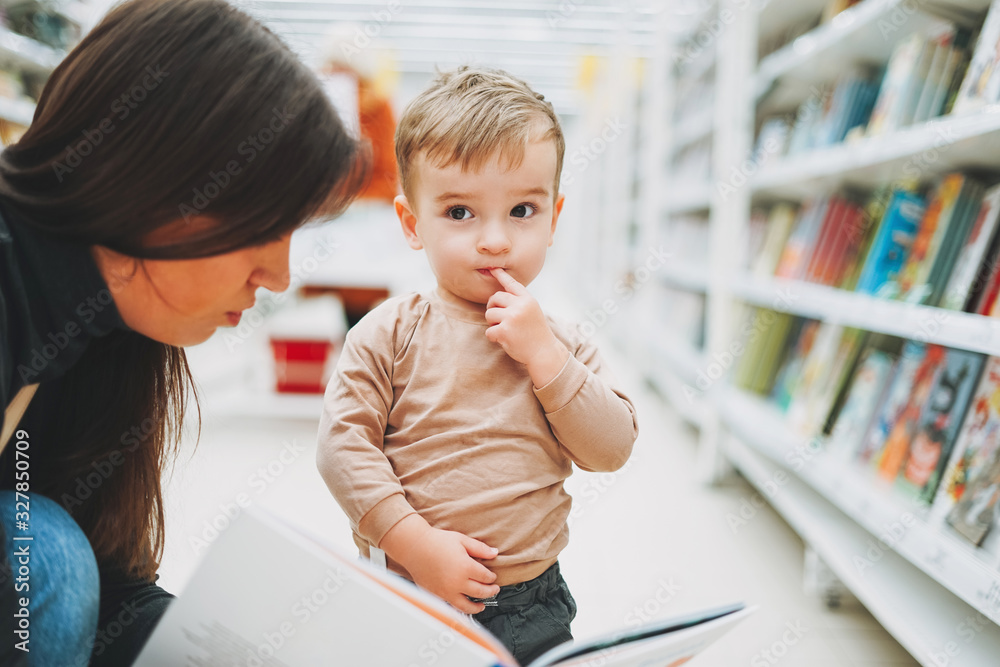 Cute baby boy toddler child in bookstore with his mother with open book ...