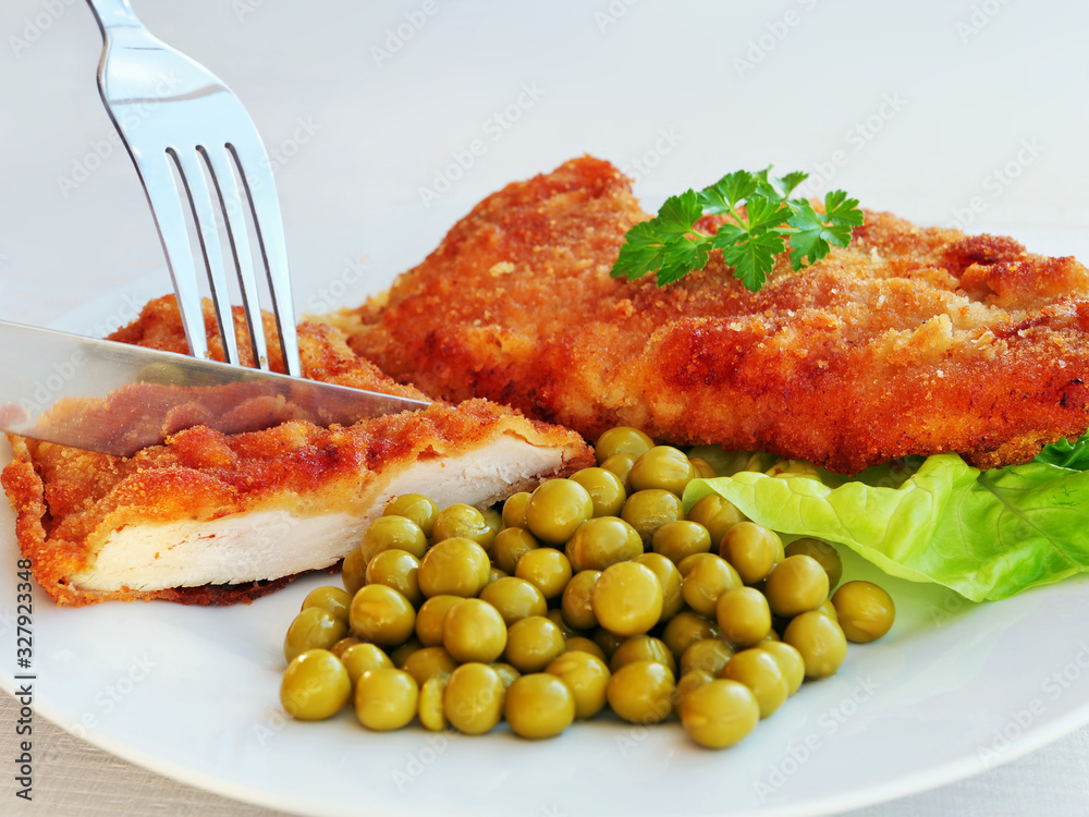 Cutting a piece of crispy breaded chicken cutlet with a fork and knife ...