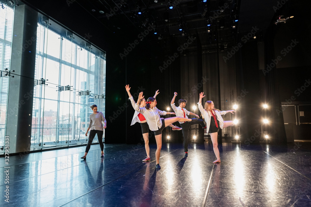 Female dance instructor watching jazz dancers rehearsing in studio ...