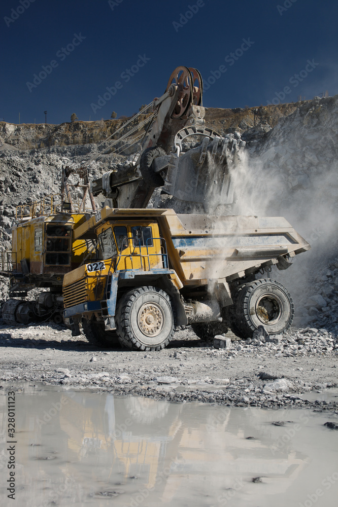 Excavator during the loading of rock ore into the body of a heavy duty ...
