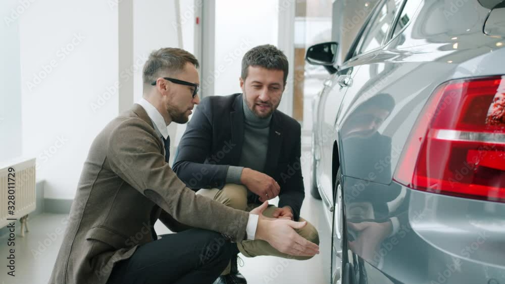 Professional salesman is speaking about new car model in motor showroom ...