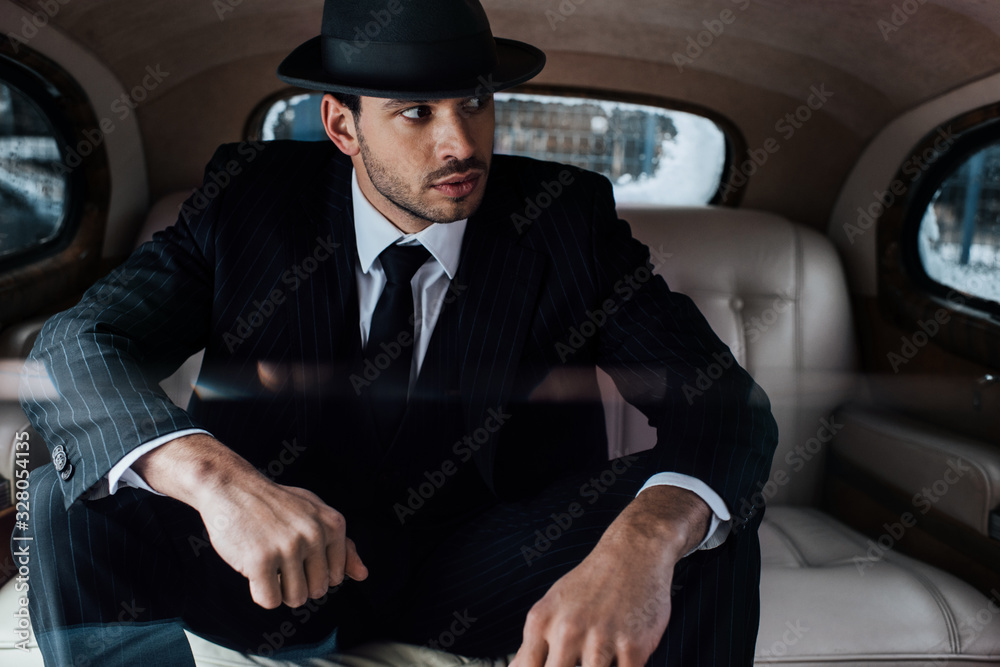 Selective focus of tense mafioso in black suit and felt hat in retro ...