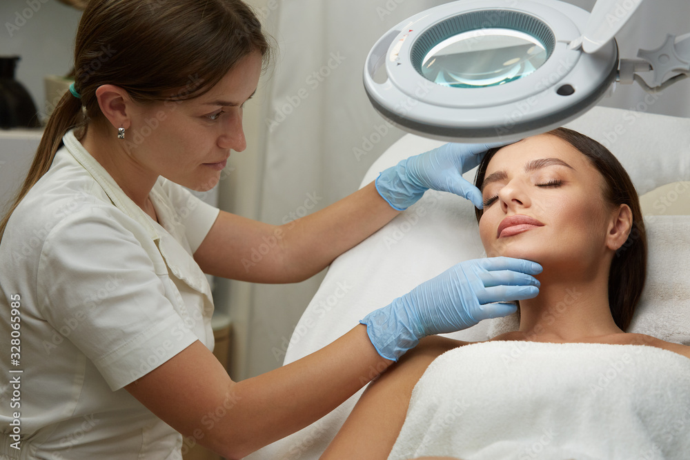 professional cosmetologist working with beautiful woman face in blue ...