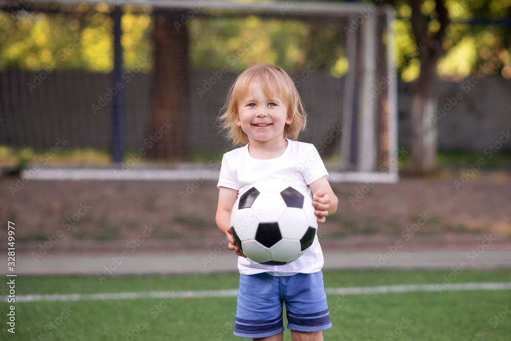 Happily smiling blonde toddler boy standing in football field (stadium ...