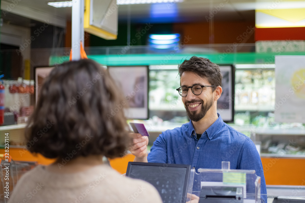Smiling man giving credit card to cashier. Customer talking with cahier ...