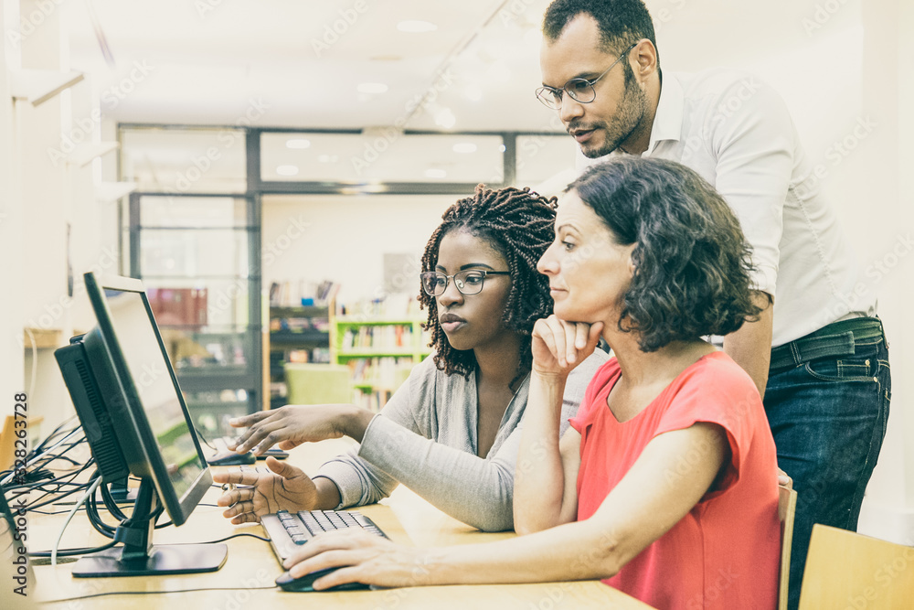 Foto de Tutor helping students in computer class. Man and women sitting ...