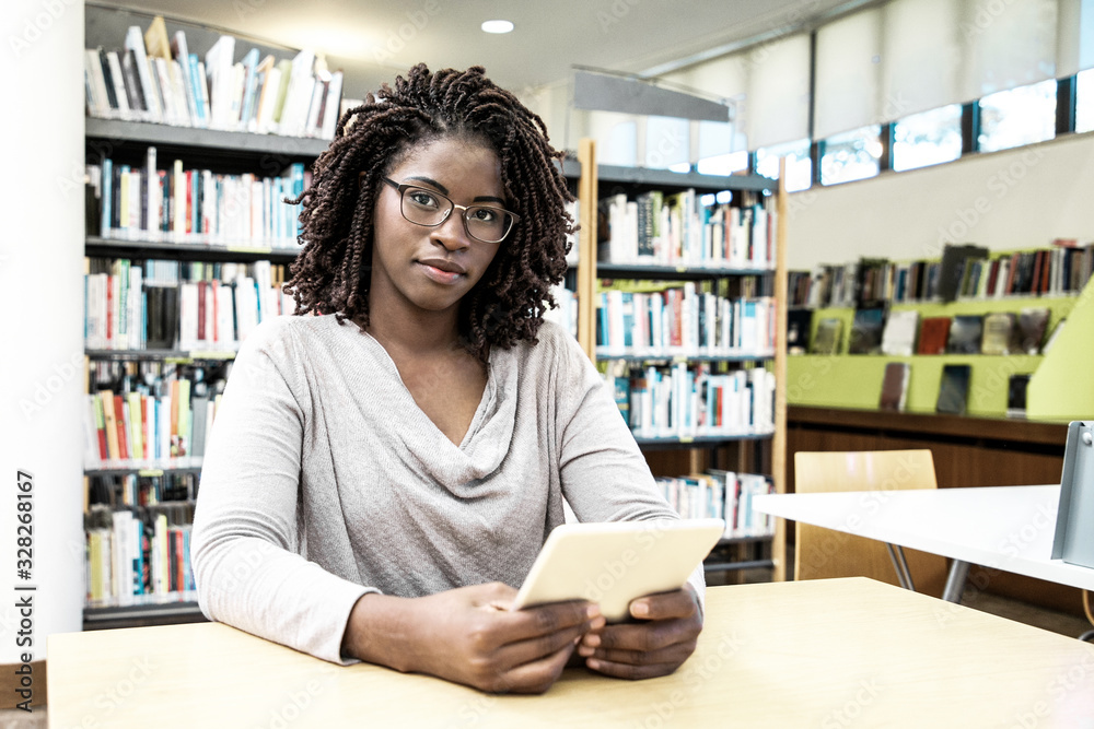 Positive female student using wireless internet connection in library ...