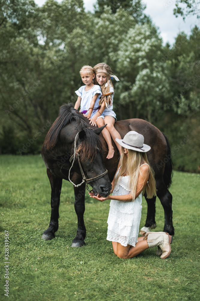 Happy family, mother with two children cute daughters riding a horse ...