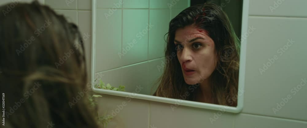 Young woman looking in the mirror, washing her face, bleeding head and ...