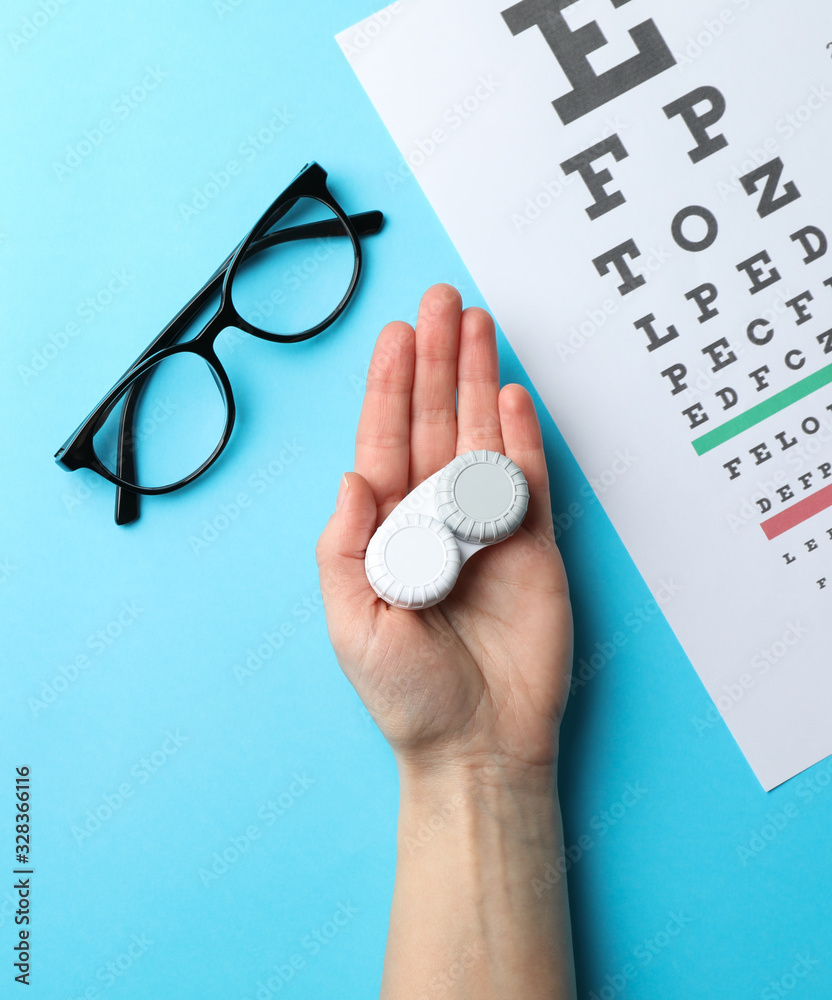 Hand with contact lenses, glasses and eye test chart on blue background ...