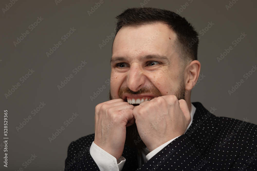 Puzzled fearful handsome bearded man keeping fists near his chin ...