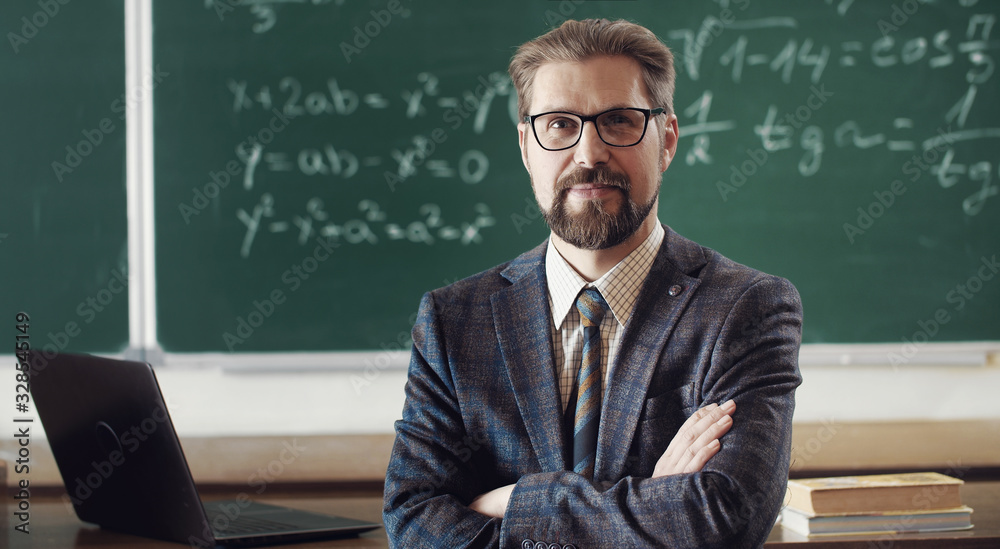 Portrait of smiling mature teacher in classic suit and eyewear standing ...