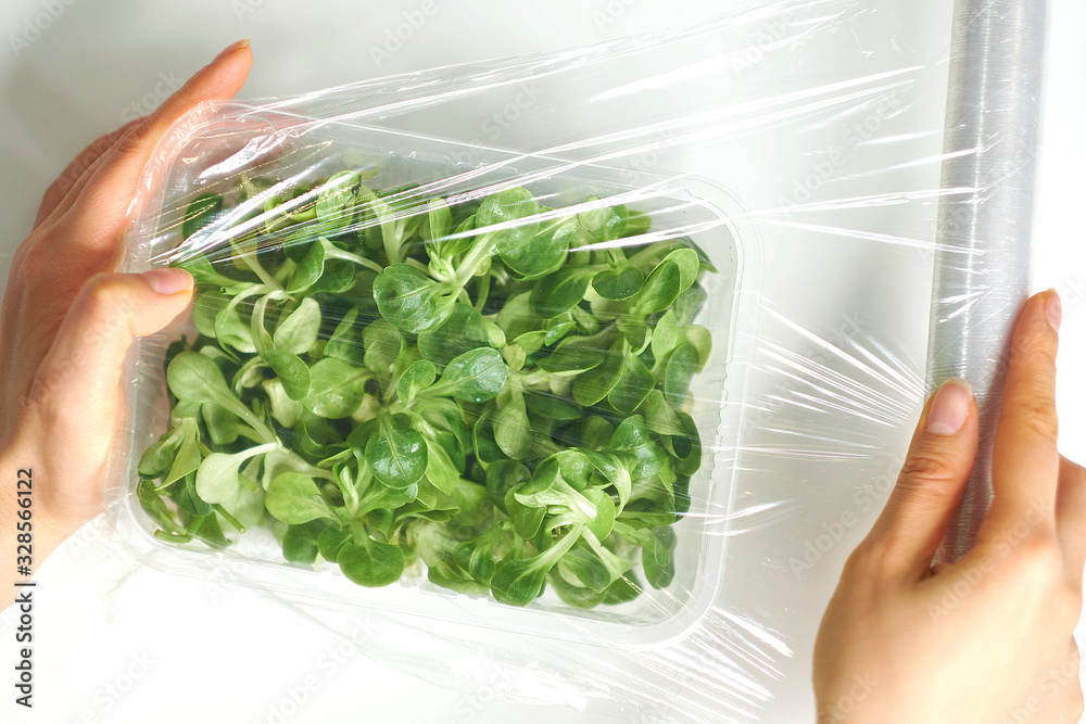 Woman using food film for food storage on a white table. Roll of ...