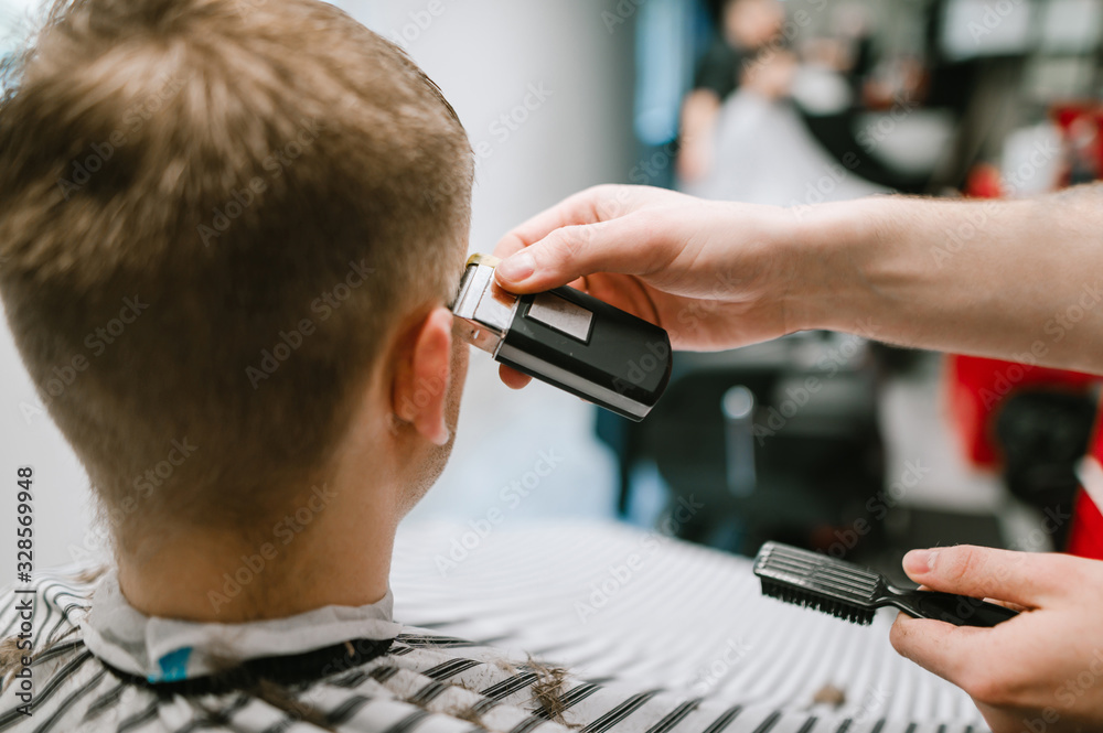 Barber's hand with a trimmer cuts the hair on a young man's temple ...