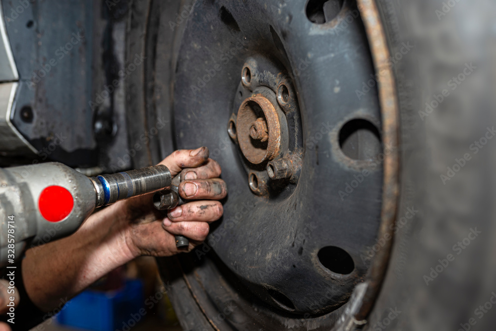 The car mechanic bolts the steel car wheel with a pneumatic wrench in a ...