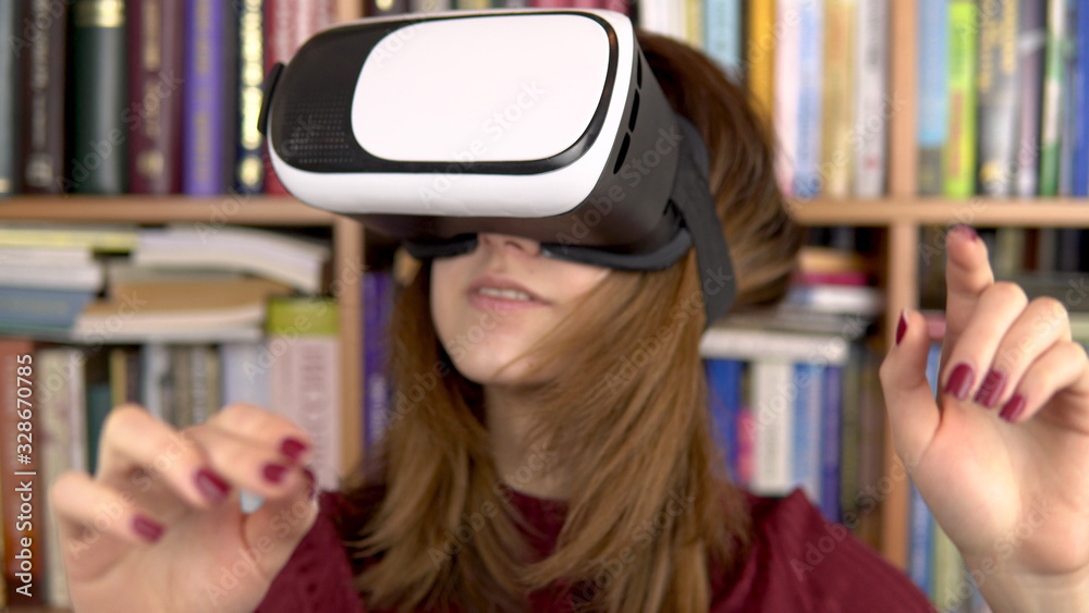 Young woman in VR glasses in the library. A woman with a VR helmet on ...