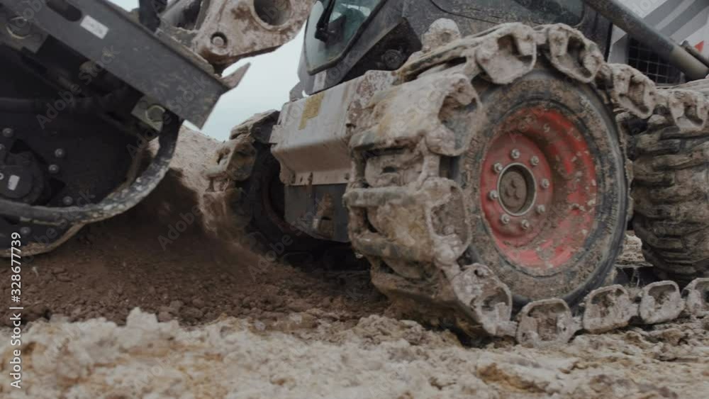 A small tractor with caterpillars on wheels carries out excavation work ...