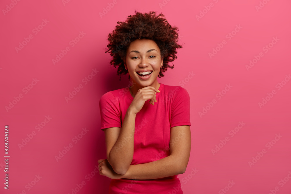 Indoor shot of lovely woman giggles happily, looks straightly at camera ...