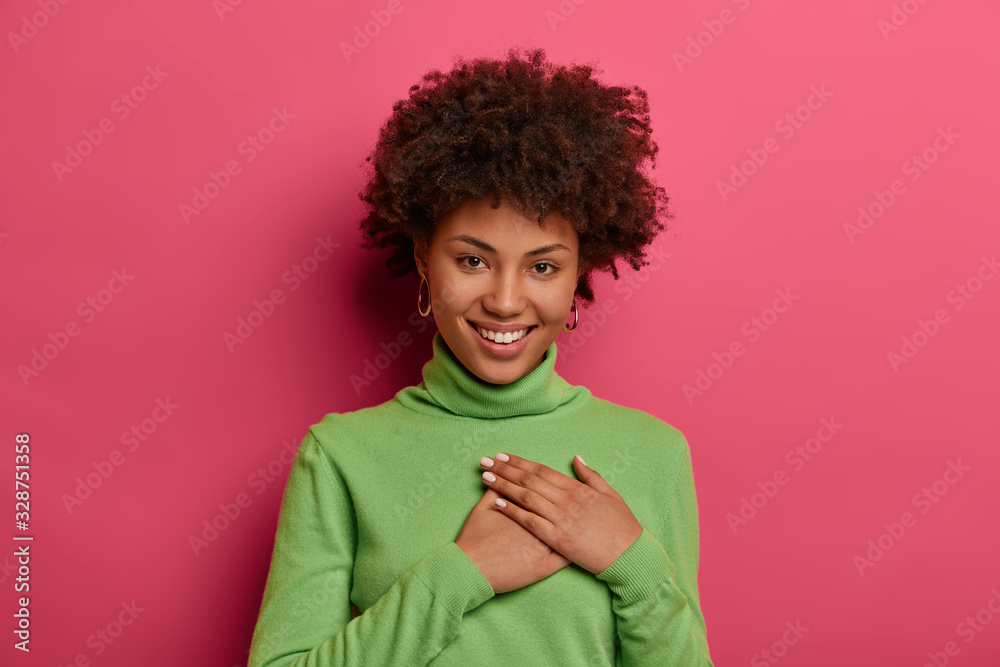 Positive young woman feels thankful, keeps hands pressed to heart ...