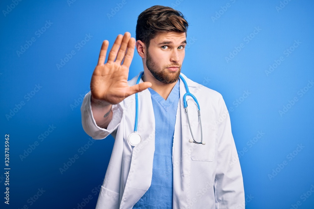 Young blond doctor man with beard and blue eyes wearing white coat and ...