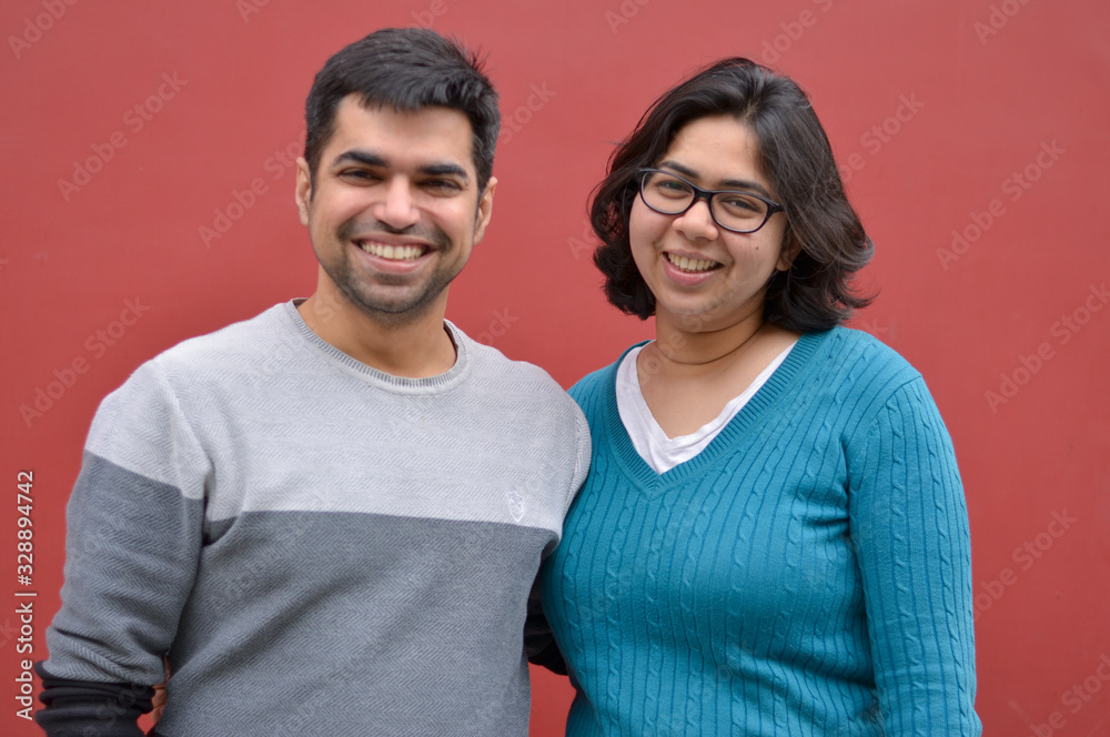 Young Indian working professional couple smiling against a red wall ...