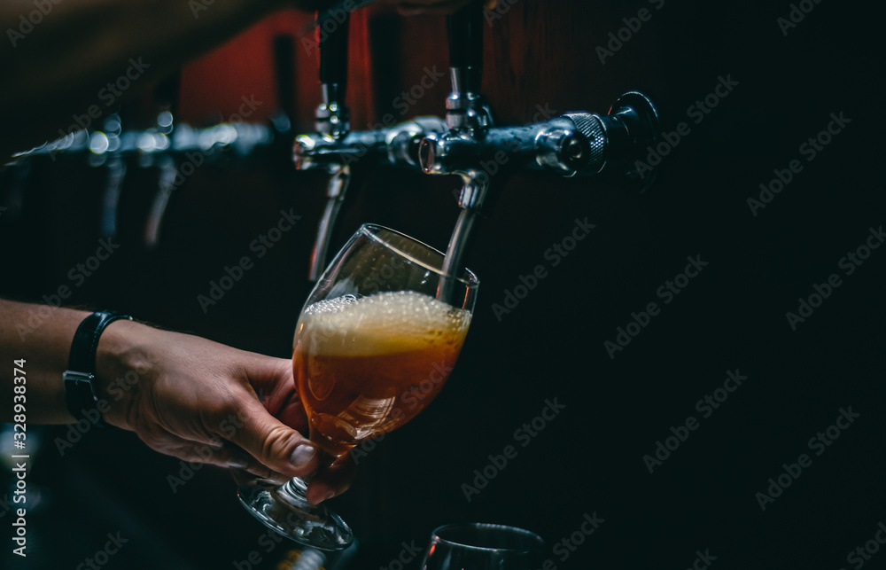 bartender hand at beer tap pouring a draught beer in glass serving in a ...