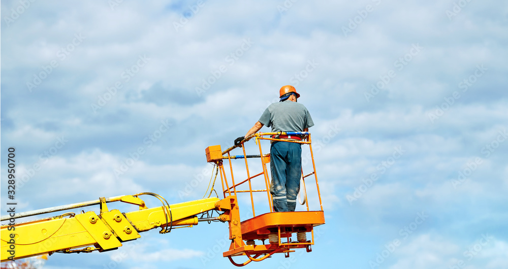 Worker in cherry picker bucket at height wearing hardhat and safety ...