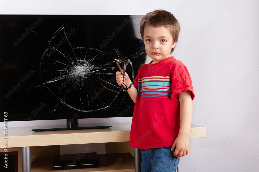 Frightened little boy standing in front of a TV with broken screen holding a slingshot Stock ...