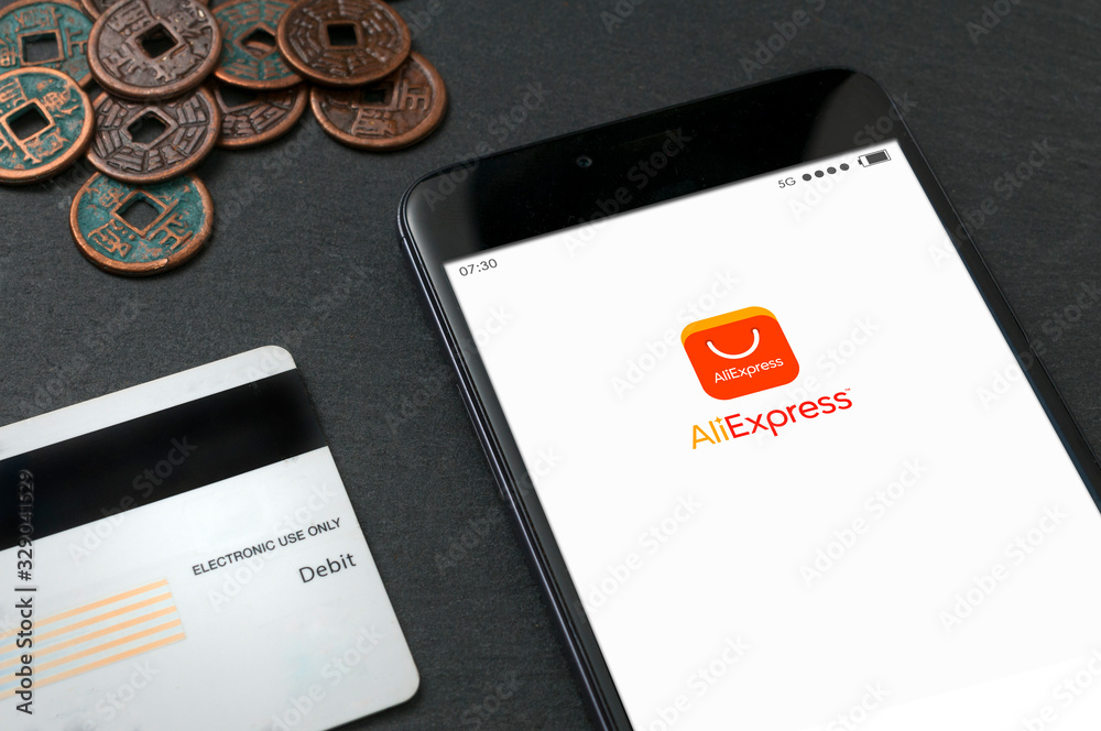 Aliexpress logo on smartphone screen next to a debit card and some ...