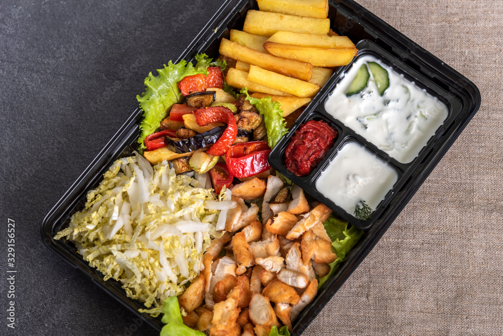 Traditional doner kebab in a black plastic container, sour cream, fried ...