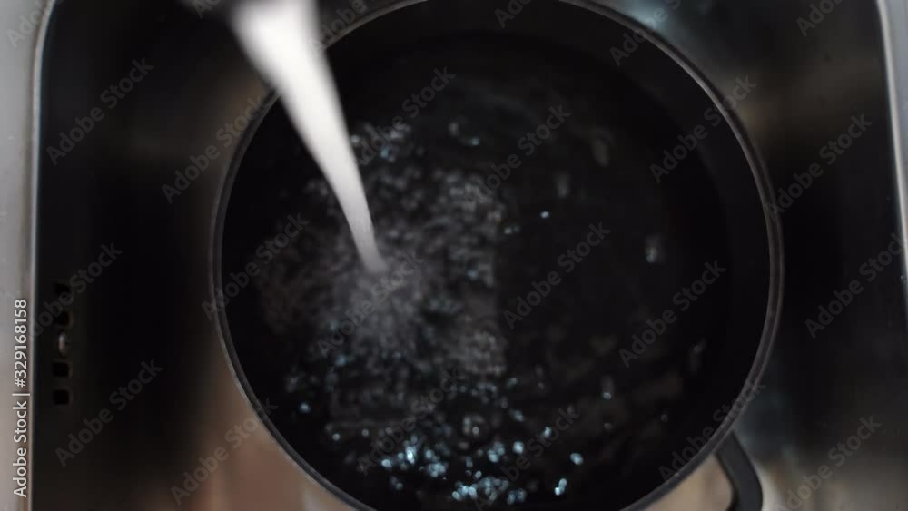 Black stainless cooking pan lying in the sink and pure water flowing in ...