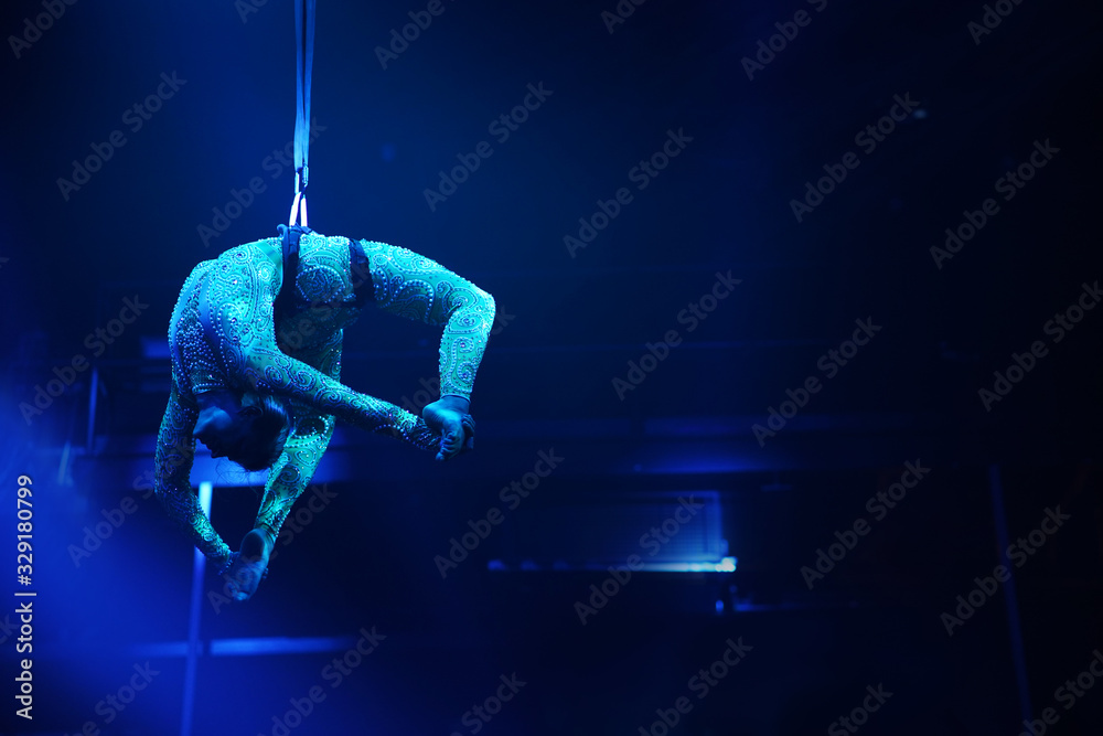 Flexible young woman make aerial performance , blue light, flexible ...