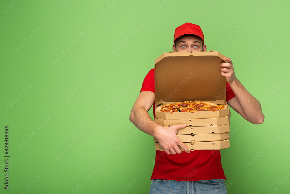 shocked delivery man in red uniform hiding behind pizza boxes on green ...