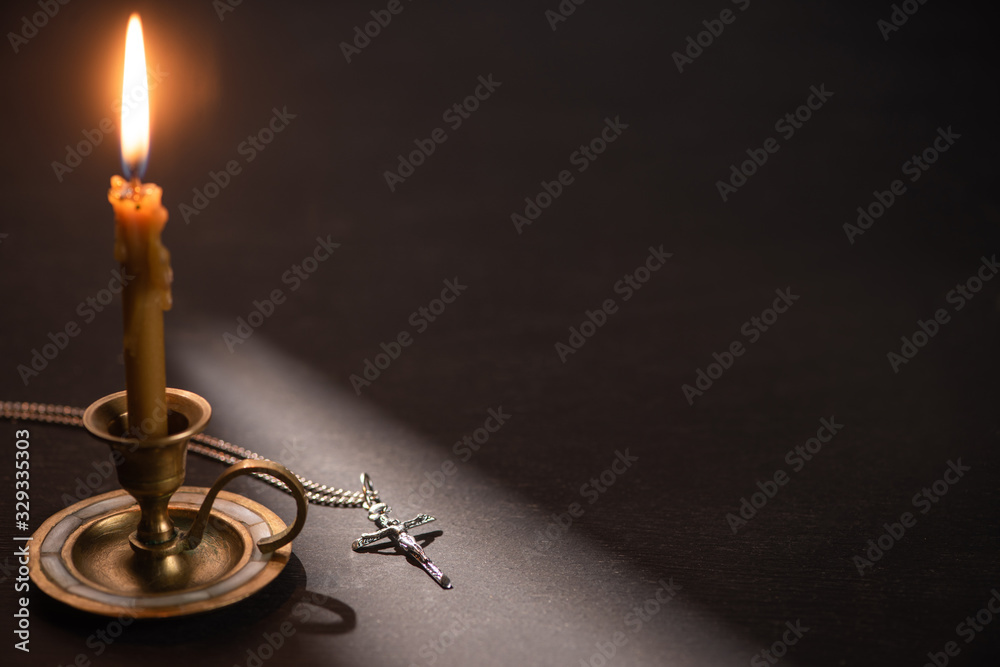 church candle in candlestick burning near catholic cross in dark with ...