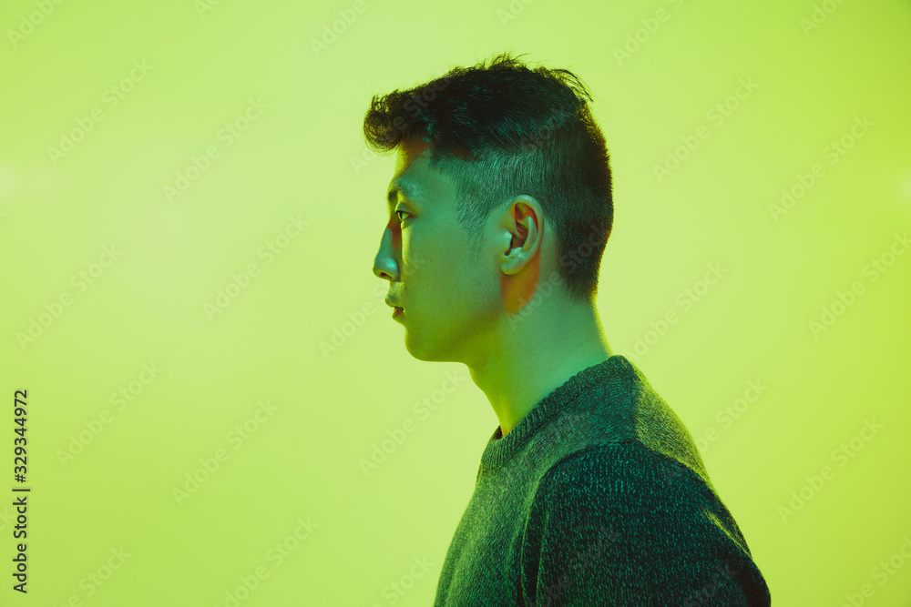 Portrait of a guy with colorful neon light on yellow studio background ...