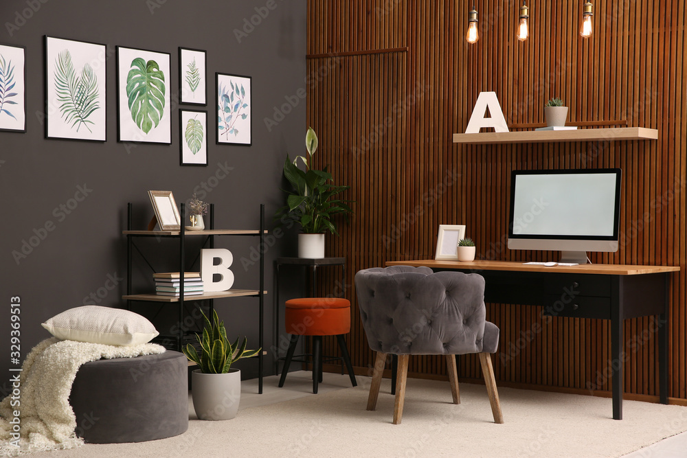 Comfortable workplace with computer near wooden wall in stylish room ...
