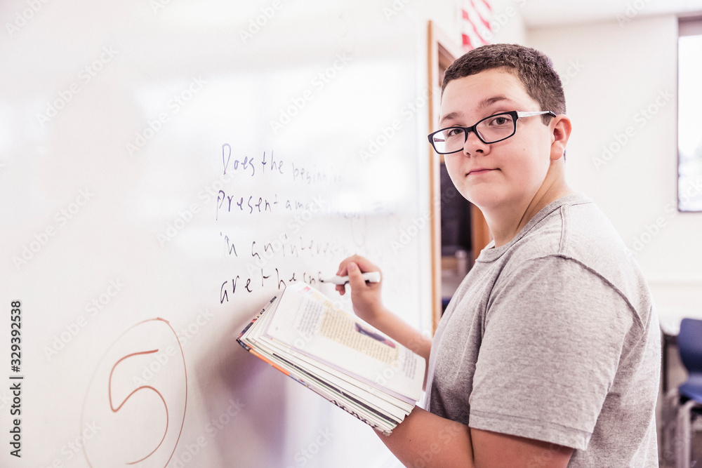 School boy writing a math formula on the white board in class . Red ...
