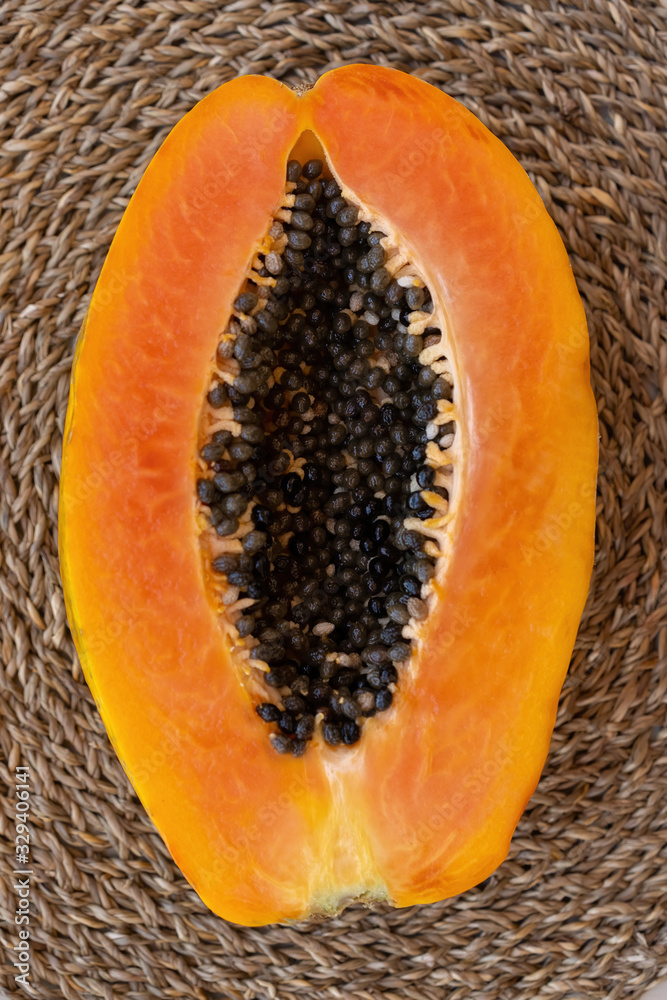 Tropical papaya fruit of orange color in a cut form with black seeds on ...