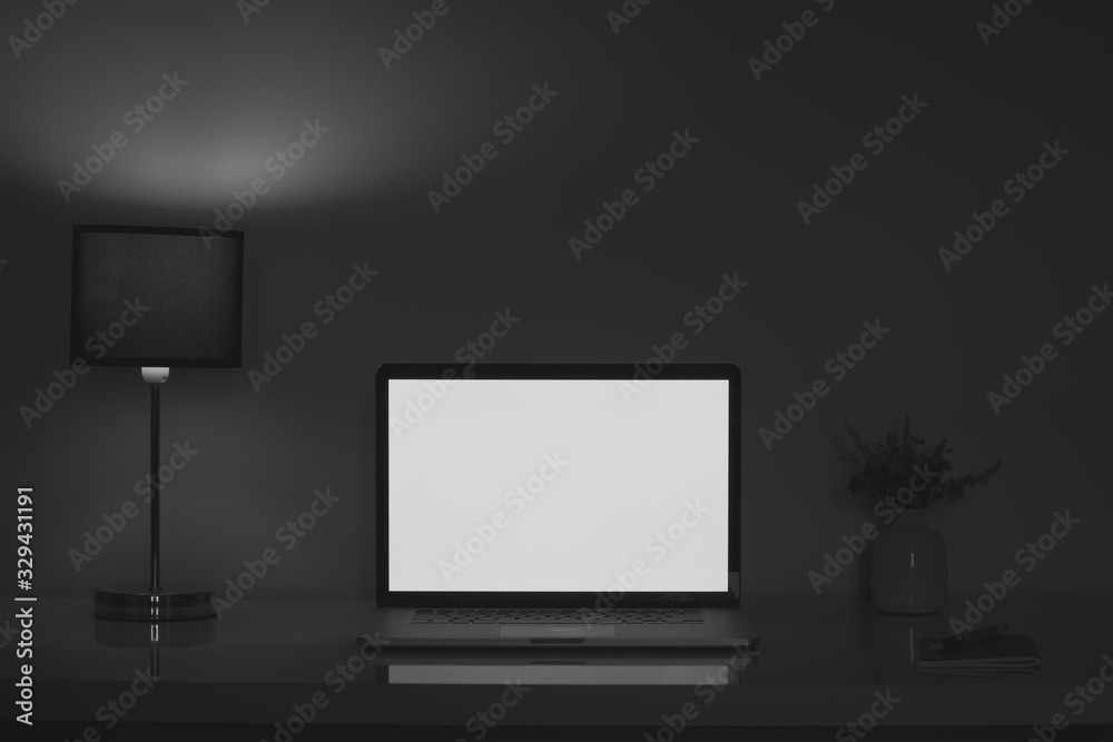 Dark home office desk at night lit by a lamp and laptop screen. Clean ...