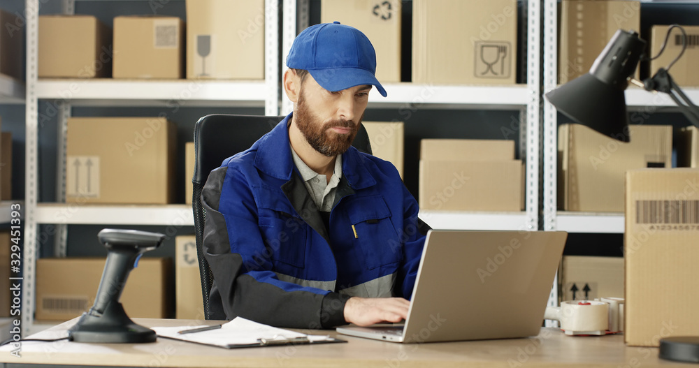 Caucasian mailman in uniform working at laptop computer in post office ...