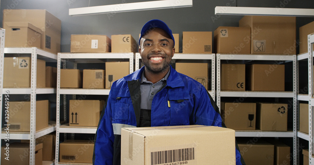 African American young joyful mailman in uniform and cap smiling ...