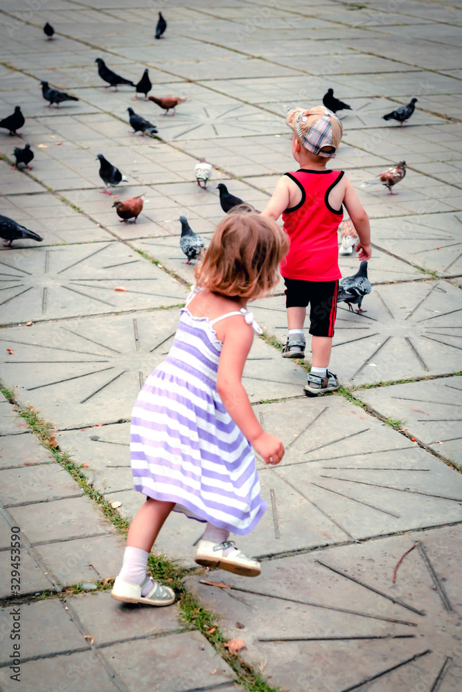 Little girl in a dress and a boy run after the birds. Stock Photo ...
