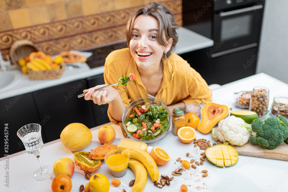 Portrait of a young cheerful woman eating salad at the table full of ...