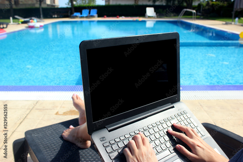 Screen mockup of laptop used by young woman laying near swimming pool ...