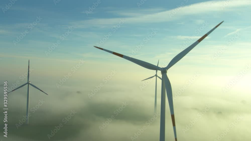 Camera flying along rotating wind wheels in backlit with ground fog ...