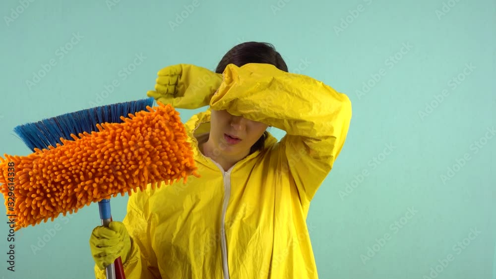Sad and tired cleaning lady in a yellow suit on a blue background. The ...