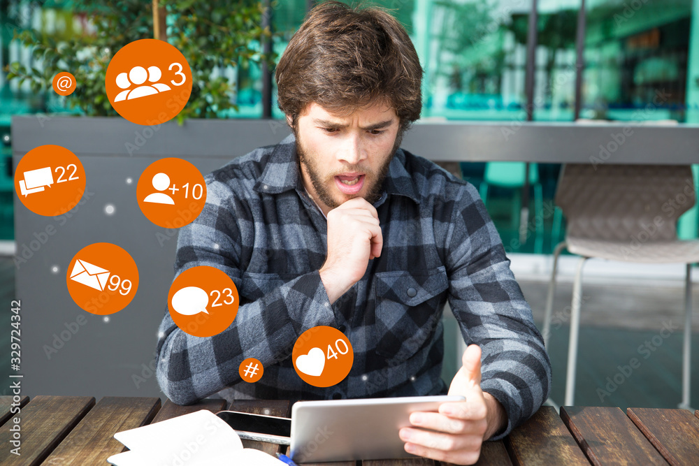 Shocked man browsing on tablet computer in street cafe. Young guy ...