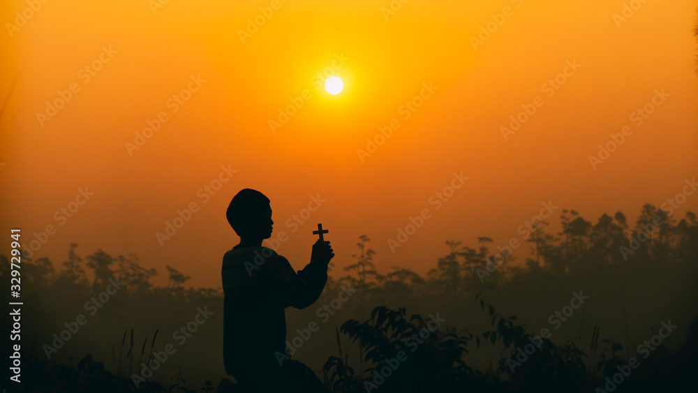 human kneeling with holding christian cross and praying at sunset ...