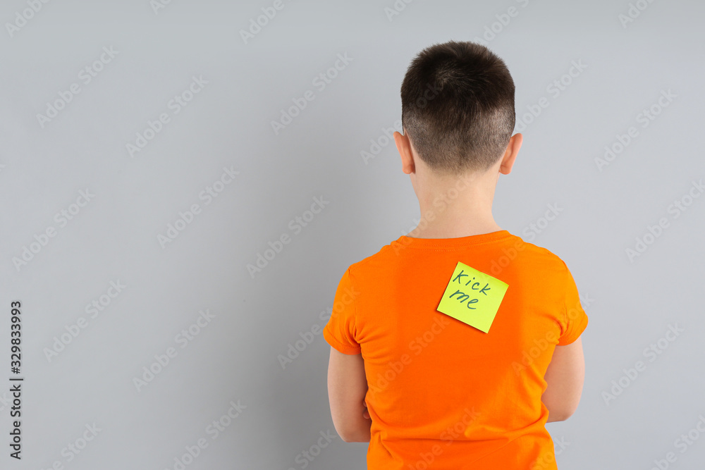 Preteen boy with KICK ME sticker on back against light grey background ...