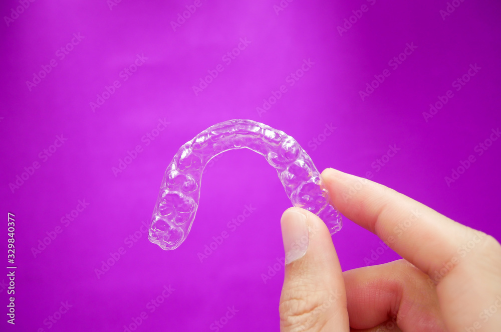 hand holding clear plastic retainer teeth that isolated on purple ...